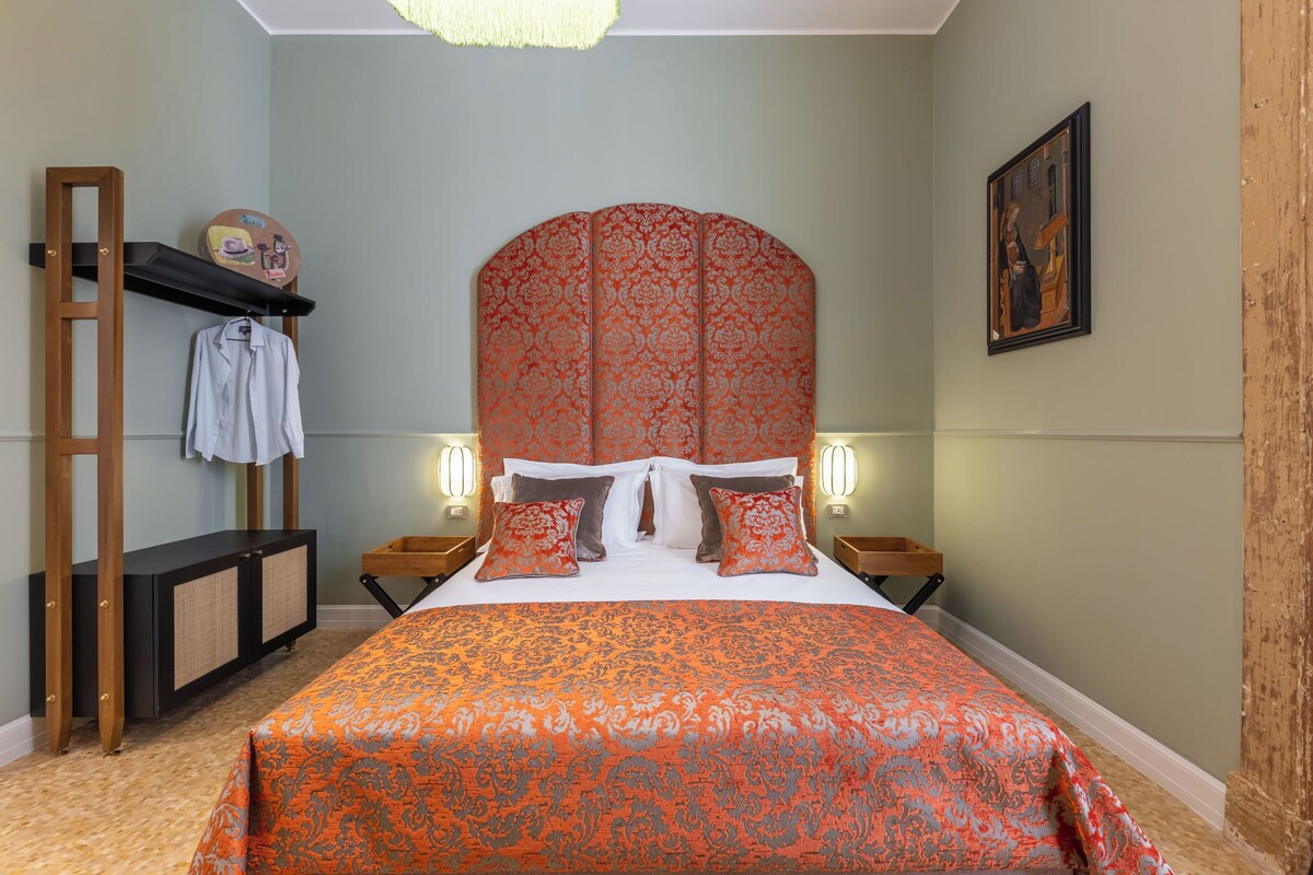 Quarto com uma cama grande, cabeceira de madeira, mesa de cabeceira, prateleira com toalha e um quadro na parede.