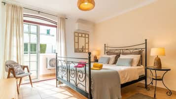 Quarto com cama, poltrona, mesa, luminária e janela.