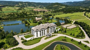 Um hotel grande, com vários andares, e um pátio central cercado por jardins ajardinados e um lago.