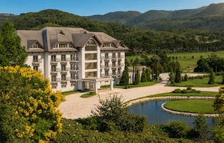 Um hotel de vários andares com um pátio central, rodeado por vegetação e um lago.