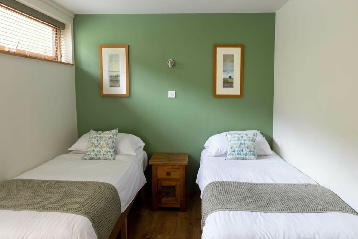 Quarto com duas camas, uma mesa de cabeceira de madeira e dois quadros na parede.