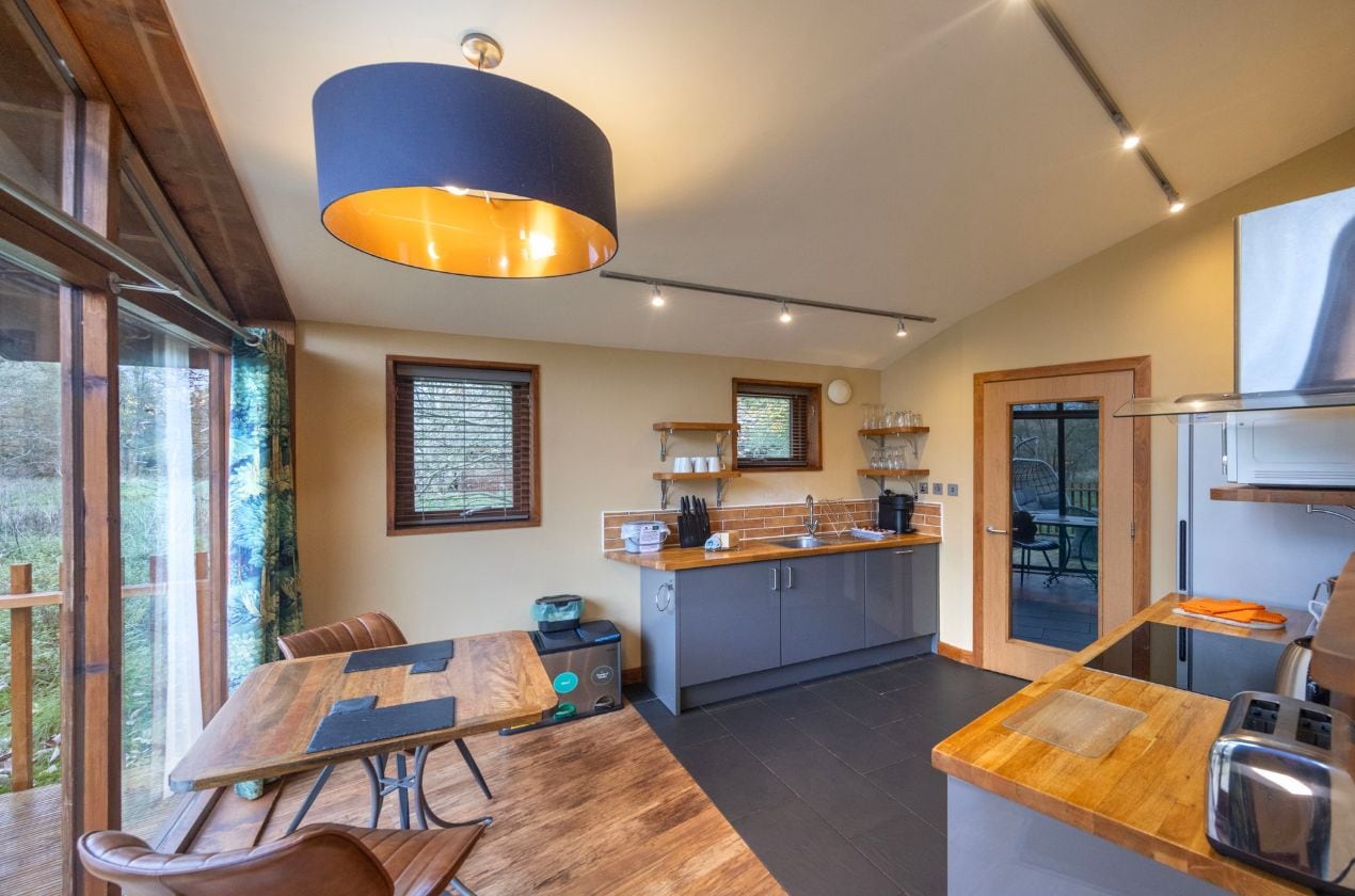 Cozinha moderna com ilha central, mesa de madeira e cadeiras, janelas amplas e luminária pendente.
