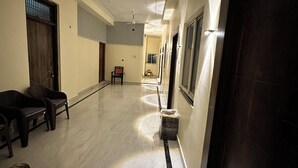 Um corredor amplo com ventilador de teto, uma porta escura à direita e uma cadeira ao centro.