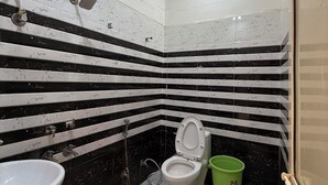 Casa de banho com sanita, lavatório, chuveiro e um contentor de lixo verde.