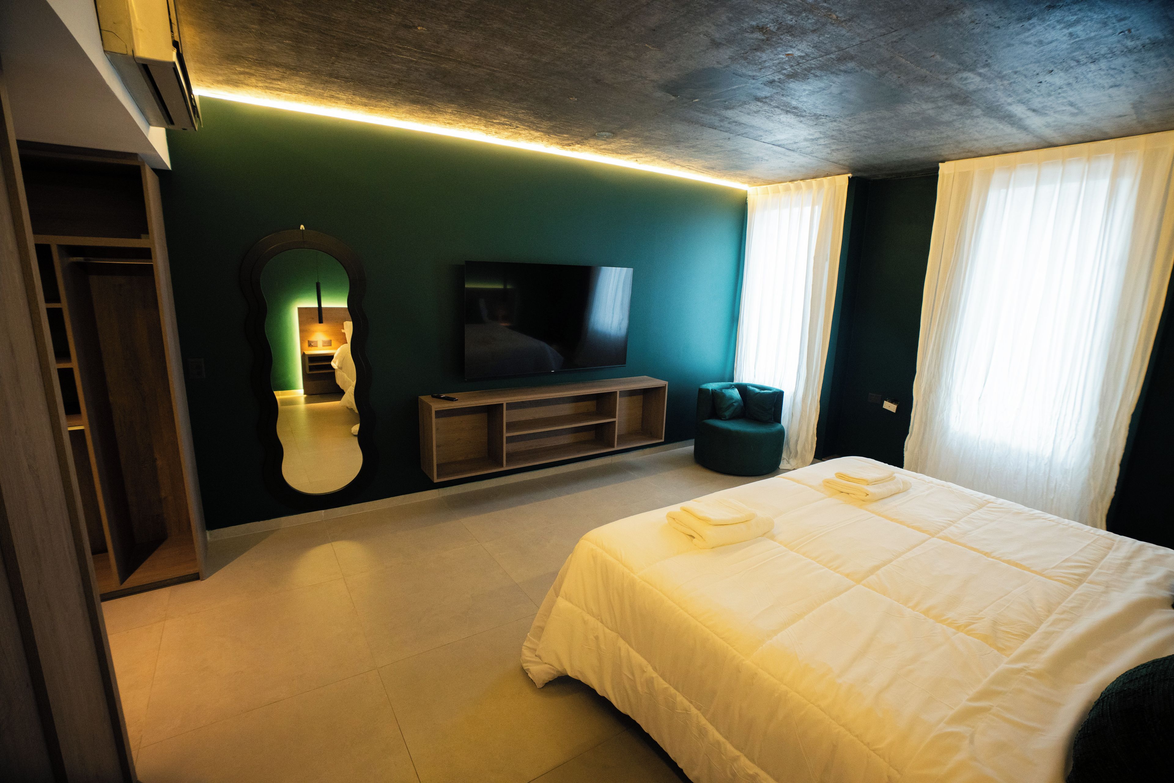 Quarto de hotel com uma cama, televisão, espelho e área de estar.