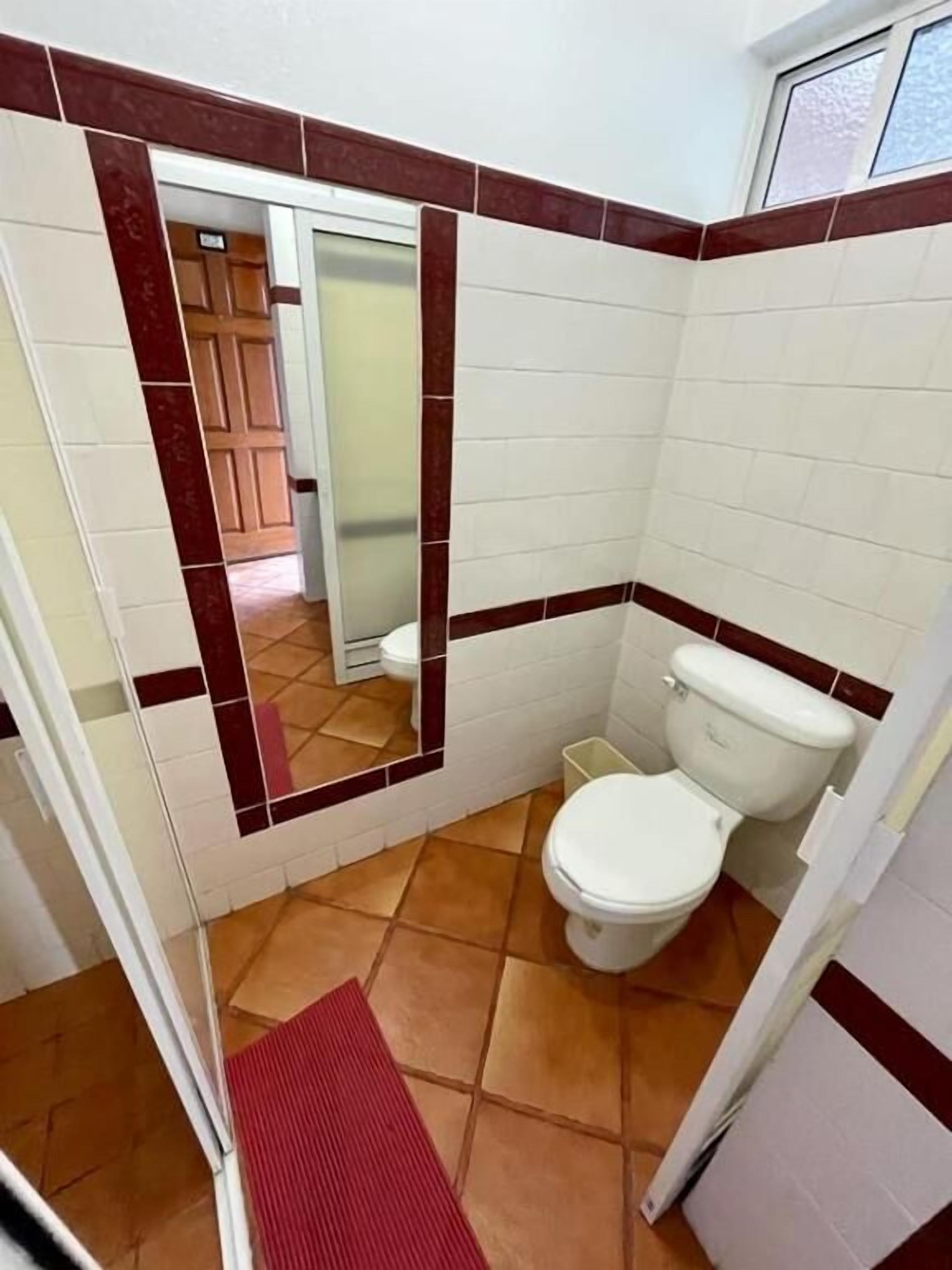 Casa de banho com sanita branca, um tapete vermelho e um espelho.