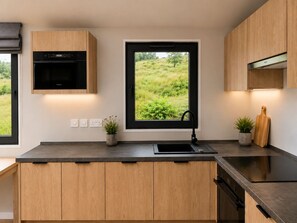 Cozinha moderna com armários de madeira, forno embutido, janela com vista para áreas verdes e uma torneira preta.