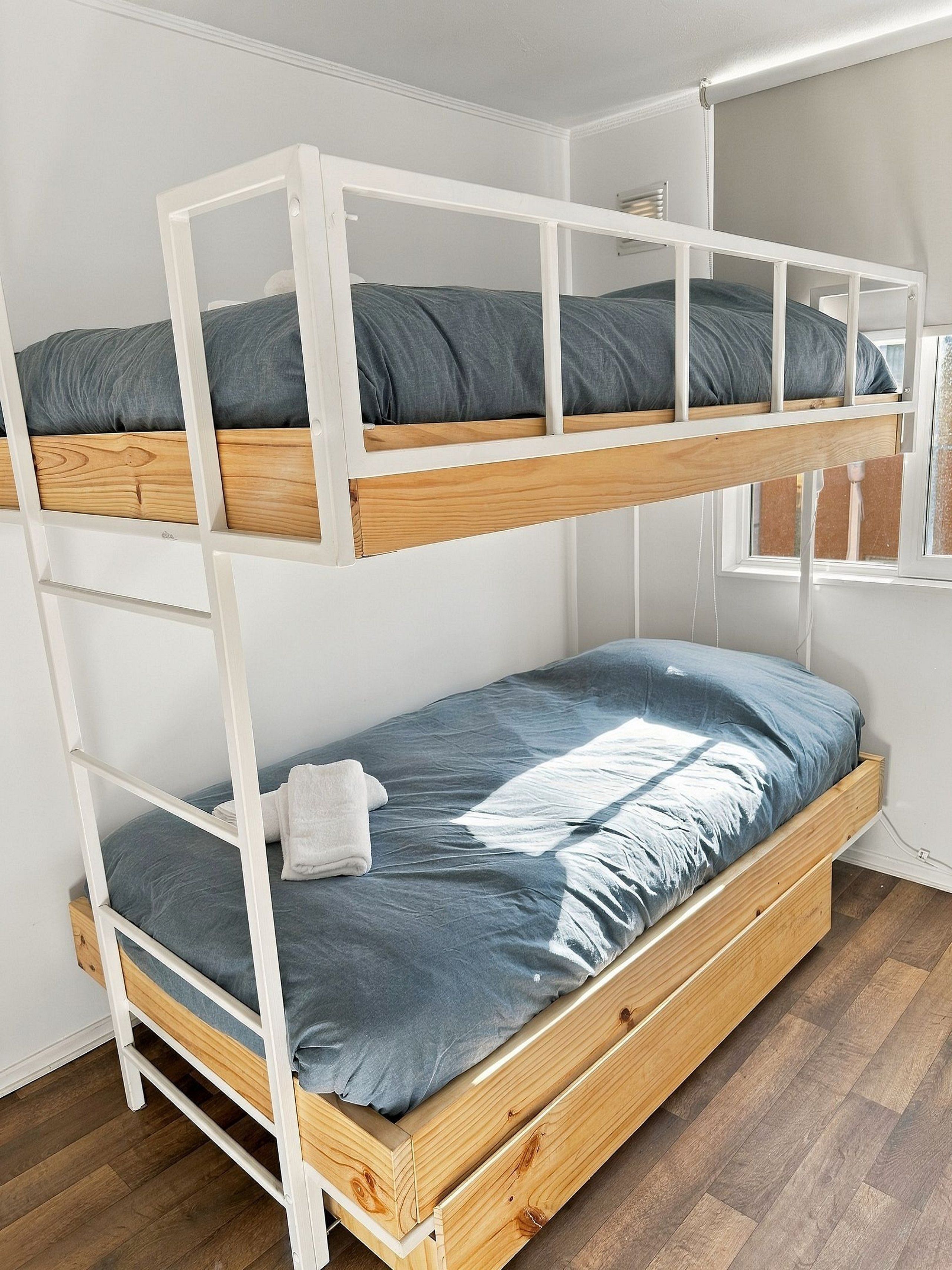 Uma cama beliche com estrutura de madeira e roupa de cama cinza.