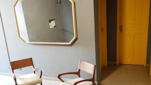 Um quarto com um espelho grande, duas cadeiras de madeira, um tapete e uma porta de madeira.