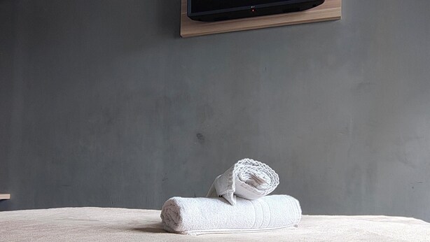 Quarto com uma cama grande, televisão de tela plana na parede e uma toalha enrolada sobre a cama.
