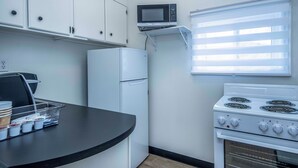 Uma cozinha compacta com eletrodomésticos brancos, incluindo micro-ondas, frigorífico e fogão.