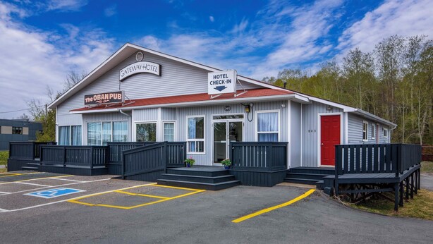 Um hotel com uma placa indicando a recepção, um pub chamado 'The OBAN PUB' no andar térreo, e uma área de estacionamento com vagas demarcadas para pessoas com deficiência.
