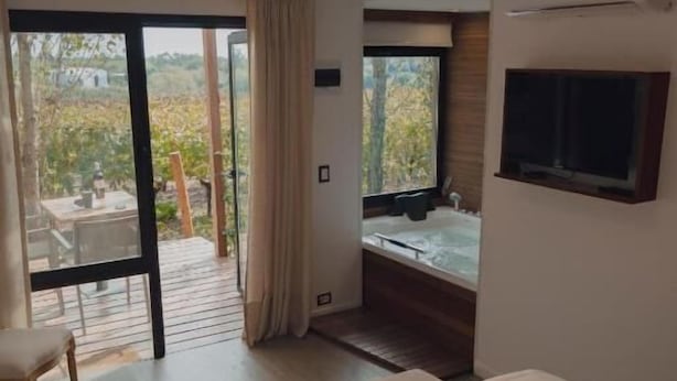 Quarto com cama grande, TV montada na parede e porta de vidro deslizante para área externa.