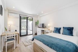Quarto com cama, escrivaninha, cadeira e porta de vidro corrediça para área externa.