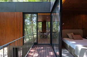 Interior moderno com deck de madeira, porta de vidro que dá para uma área de estar externa e cama com almofadas.