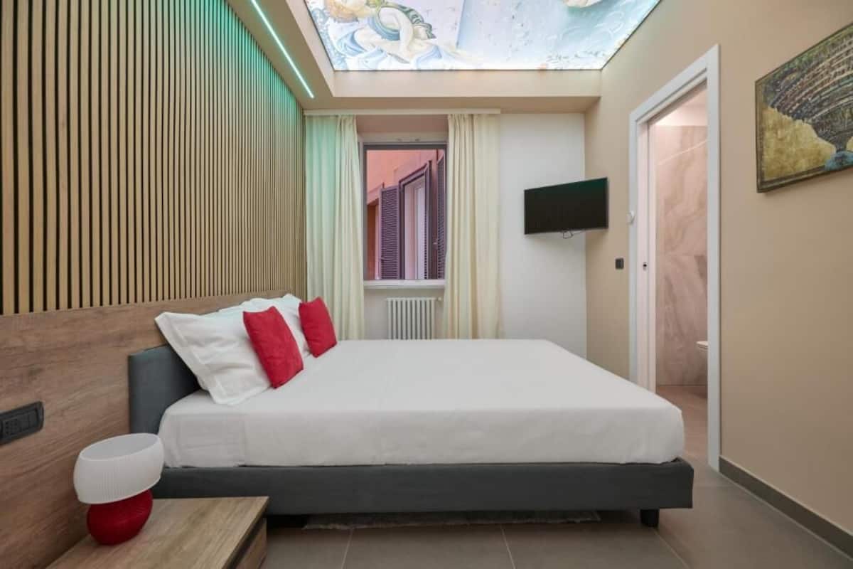 Quarto de hotel moderno com claraboia, cama com roupa de cama branca e vermelha, televisão de tela plana e painel de parede de madeira.