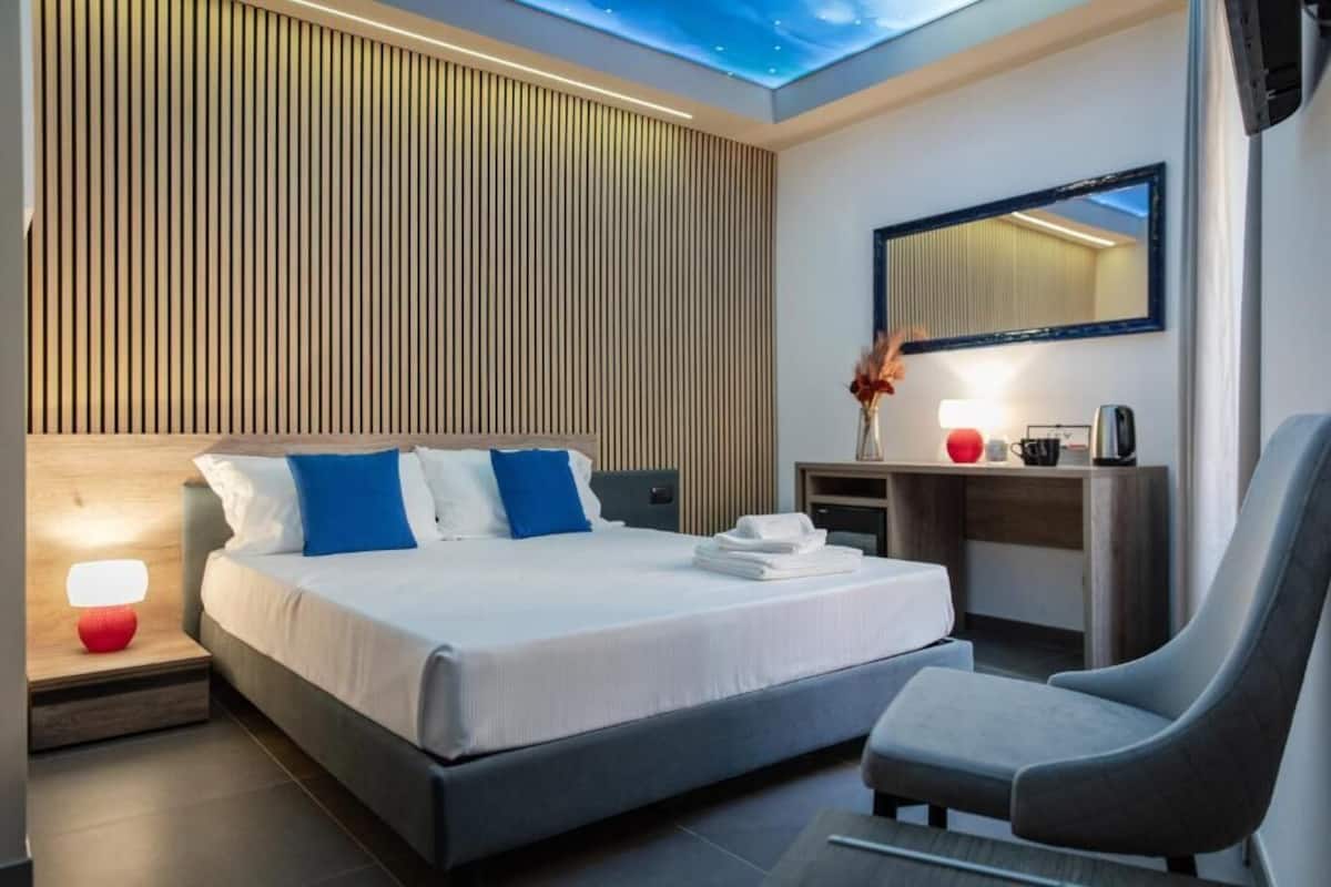 Quarto de hotel moderno com cama, escrivaninha, cadeira, mesa de cabeceira e claraboia.