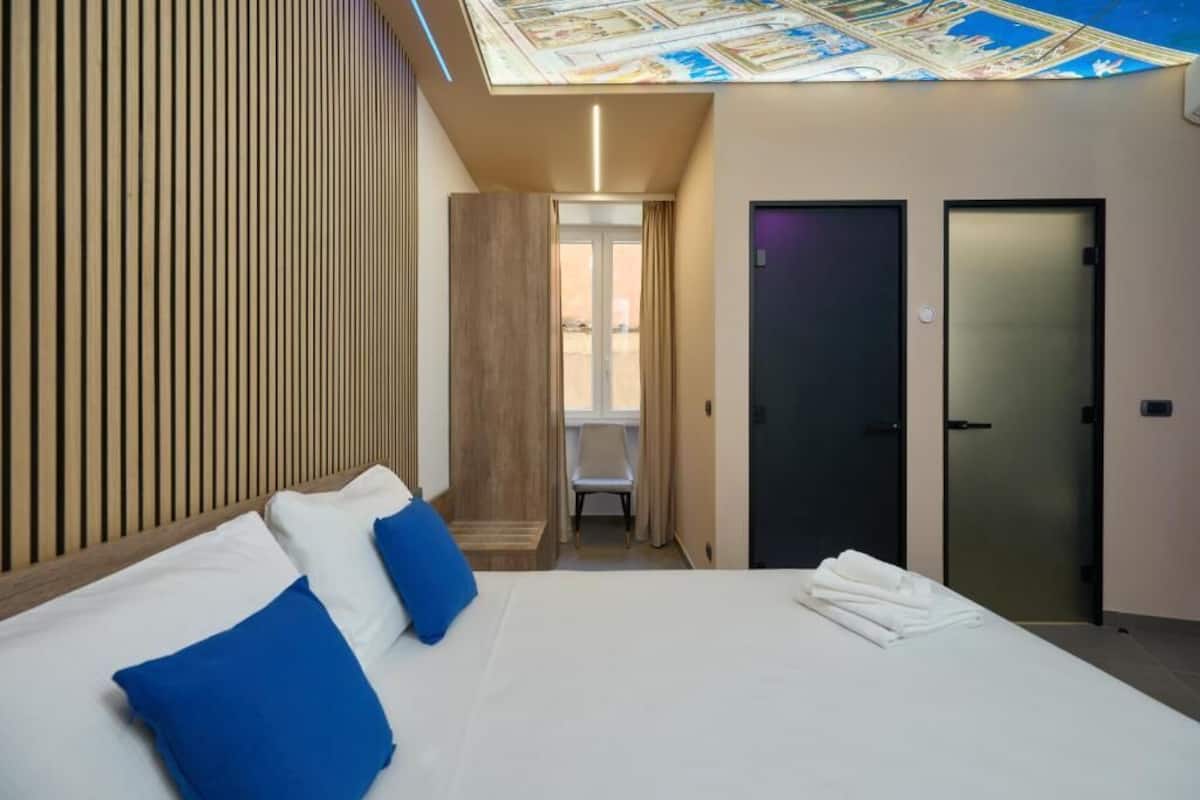 Quarto de hotel com cama, cadeira, escrivaninha e porta.