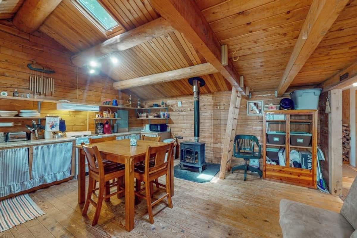 Interior de uma cabana de madeira com área de refeições, cozinha e um fogão a lenha.