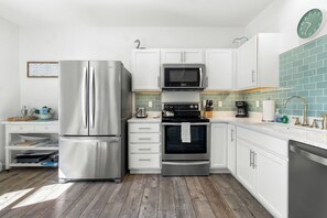 Uma cozinha moderna com eletrodomésticos de aço inoxidável, armários brancos e um painel de parede verde.