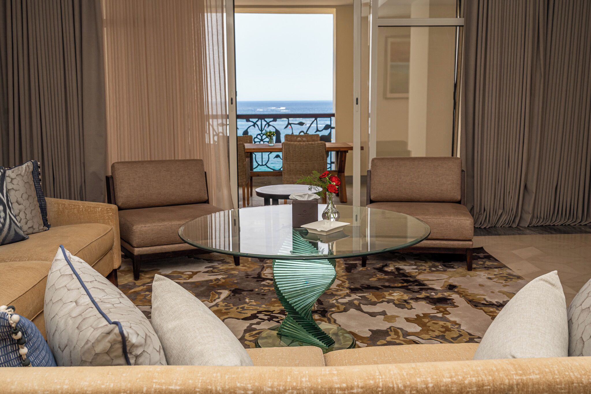 Sala de estar com mesa de centro de vidro, dois sofás e vista para o mar através de uma varanda.