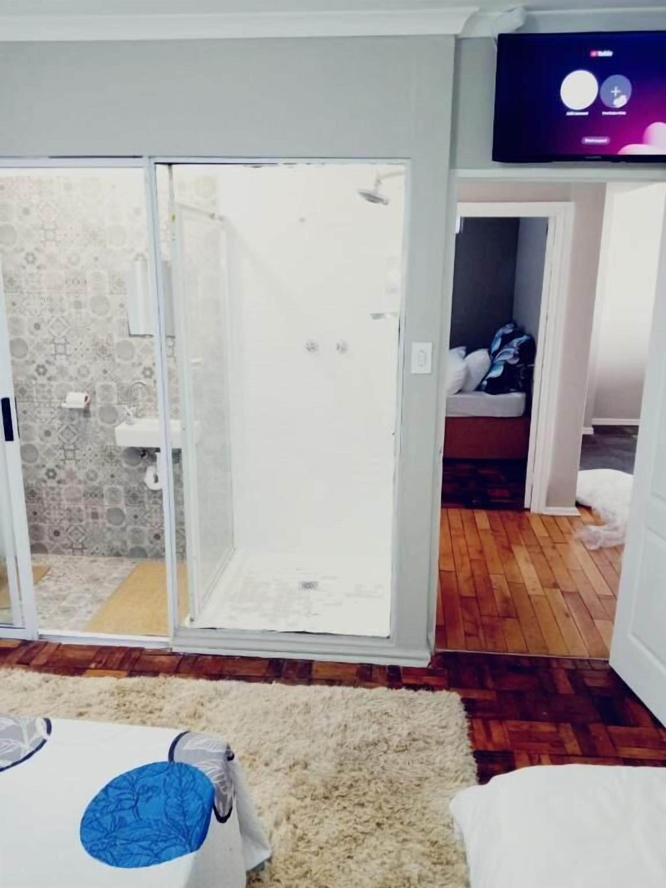 Quarto com chuveiro, cama, televisão e piso de madeira.