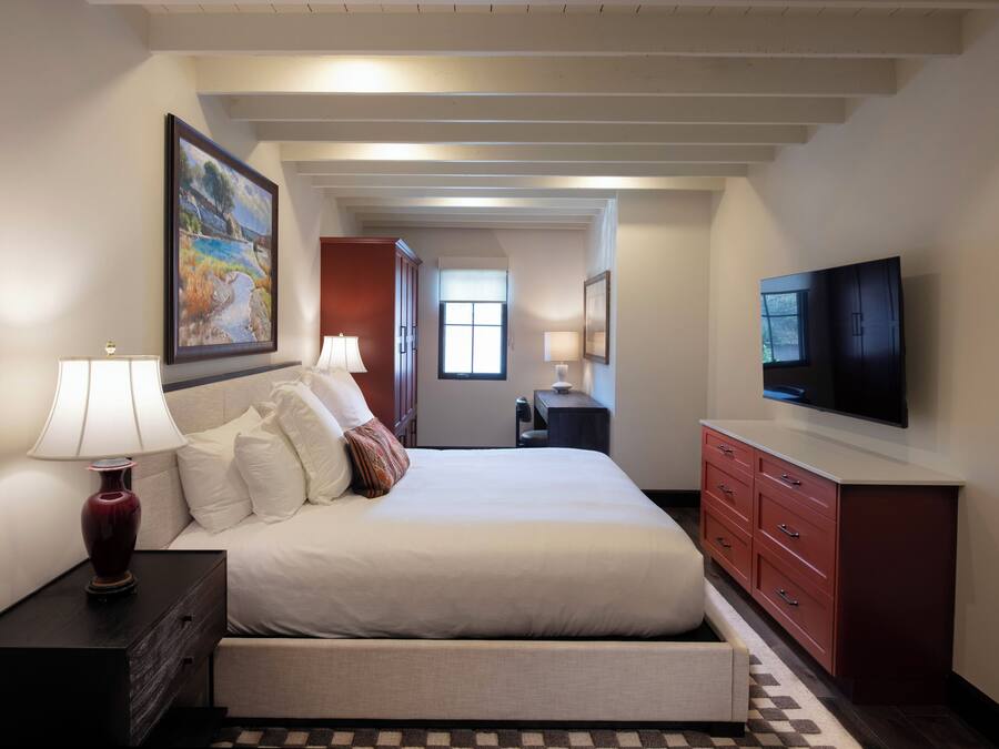 Quarto de hotel com uma cama, mesas de cabeceira, uma televisão e um quadro na parede.