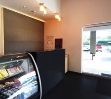 Decoração moderna com máquina de vendas automática, divisória preta e vista para carros estacionados lá fora.