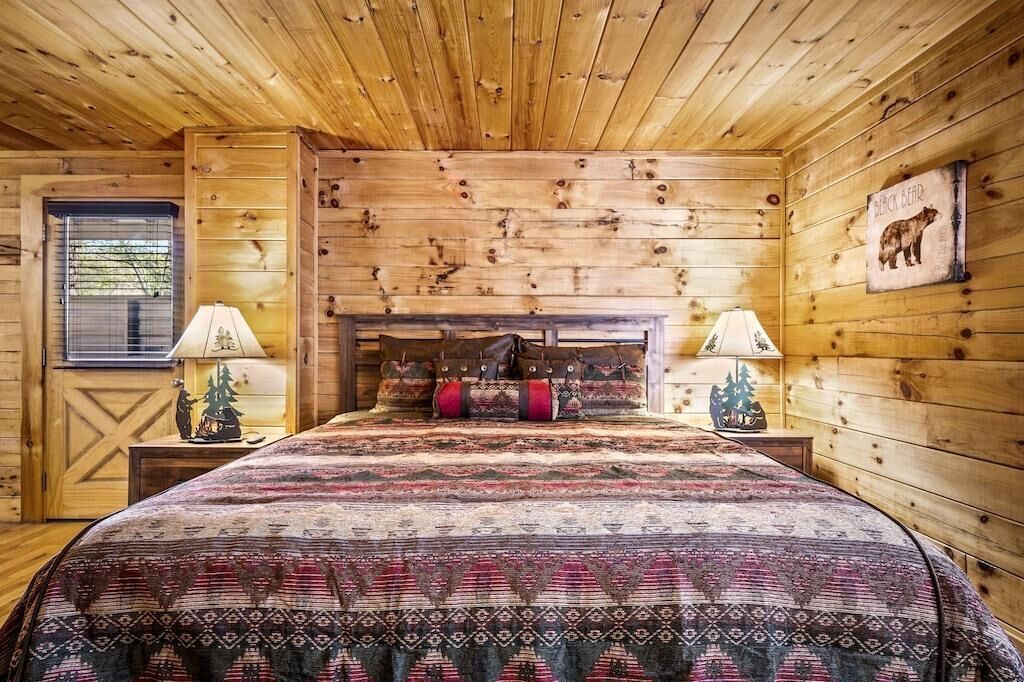 Quarto de cabana de madeira com uma cama, duas mesas de cabeceira e uma janela.