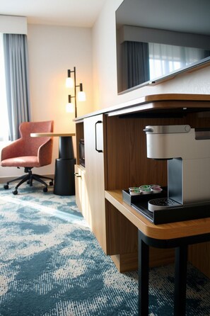Quarto de hotel com escrivaninha, cadeira, máquina de café e televisão.