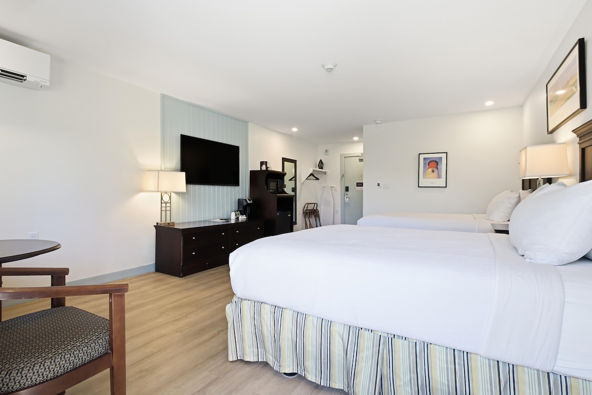 Quarto de hotel com cama, escrivaninha, cadeira, televisão e um quadro na parede.