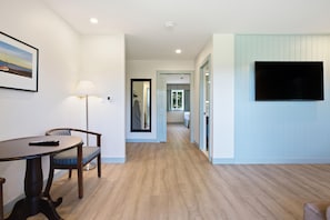 Quarto de hotel com área de refeições, televisão de tela plana fixada na parede e corredor que dá para outros quartos.