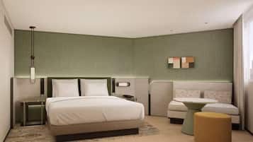 Quarto de hotel moderno com uma cama grande, uma mesinha de cabeceira, um sofá e uma pequena mesa.