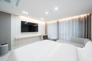 Quarto de hotel moderno com uma cama grande, televisão de tela plana na parede, uma pequena mesa redonda e um espaço de estar com sofá.