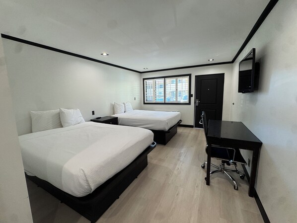 Quarto de hotel com duas camas, escrivaninha, cadeira, televisão e janela com persianas.