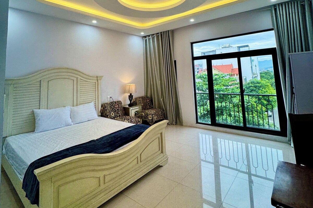 Quarto moderno com uma cama grande, luminária no teto e vista para o verde lá fora.