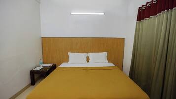 Quarto de hotel com cama, mesa de cabeceira, luminária, janela com cortinas e luminária fixada na parede.