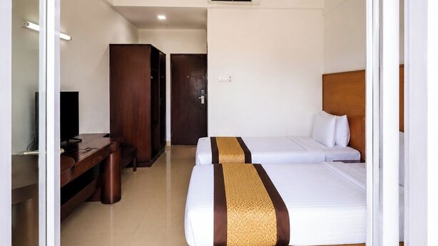 Quarto de hotel com cama, escrivaninha, televisão e ventoinha no teto.