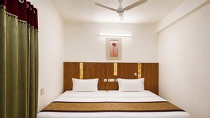Uma cama de casal com cabeceira de madeira, uma mesinha de cabeceira, um ventilador de teto e um quadro na parede.