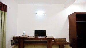 Quarto de hotel com uma escrivaninha de madeira, televisão de tela plana, garrafa de água e um armário.