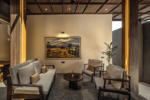 Interior moderno com sofá, poltronas, mesa de centro e uma grande pintura de paisagem na parede.