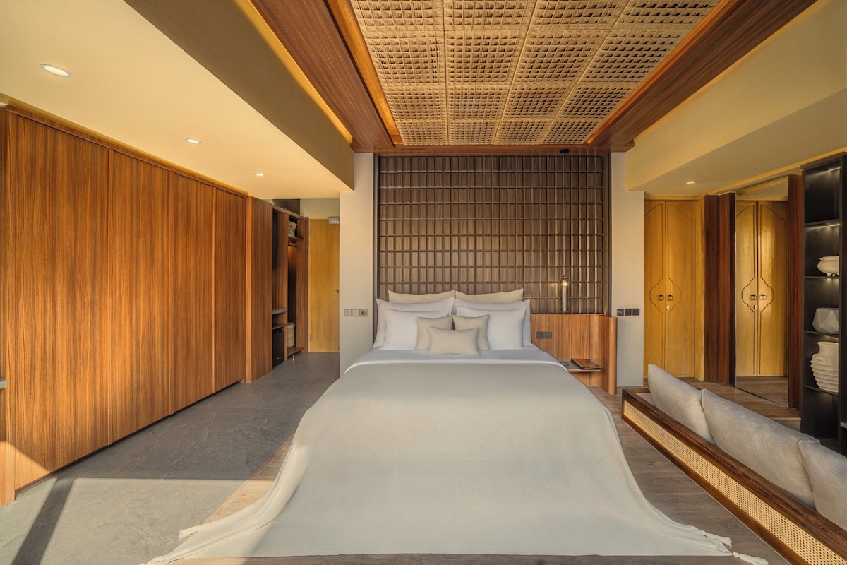 Quarto de hotel moderno com uma cama grande, guarda-roupa de madeira e um design de teto exclusivo.