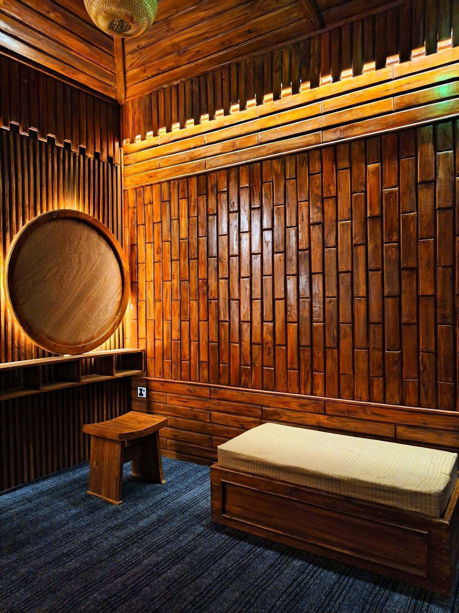 Quarto de madeira com um espelho redondo, um banquinho pequeno e um banco.