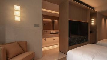Quarto de hotel moderno com sofá, cama, televisão e banheiro com espelho e pia.