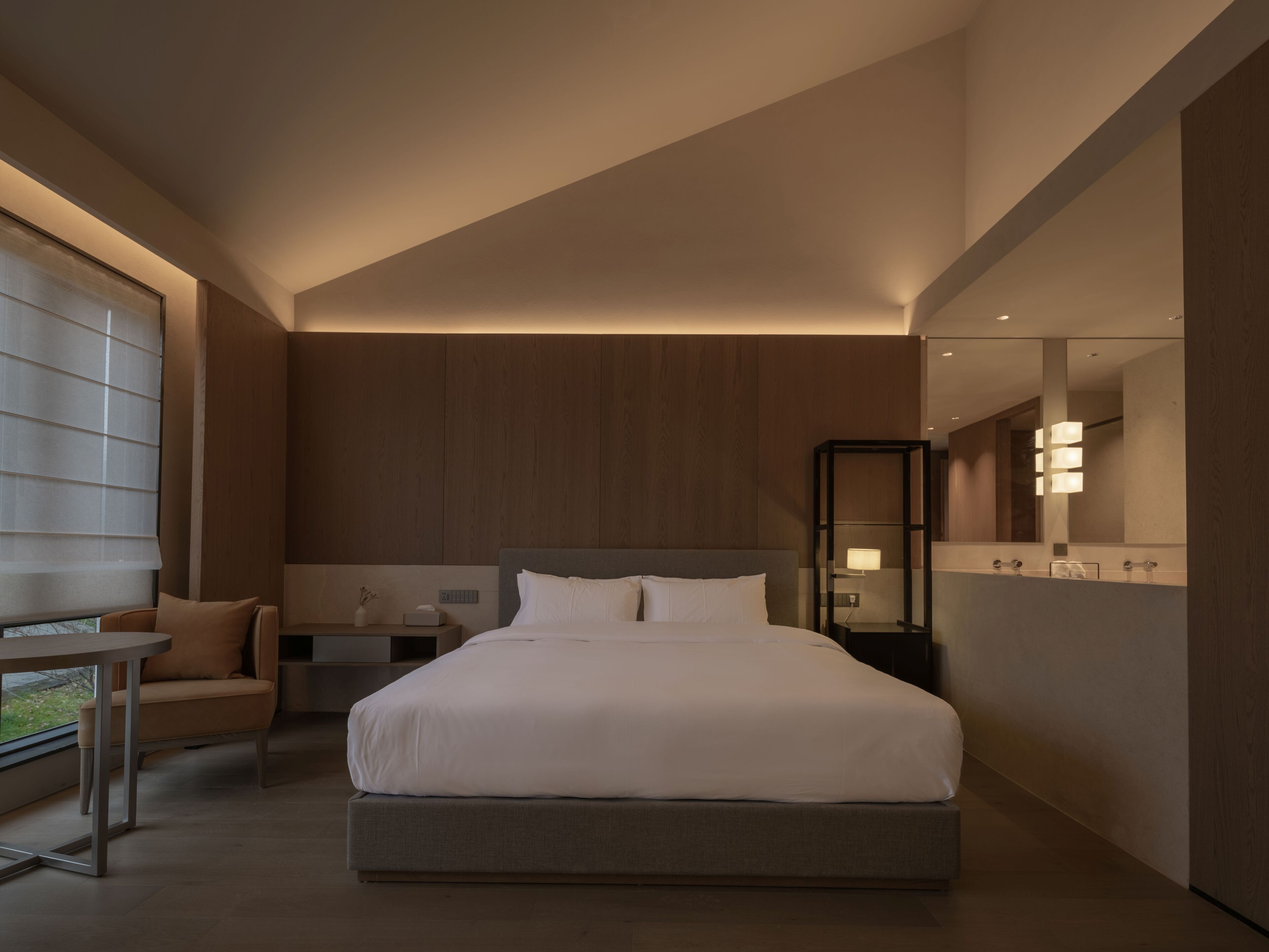 Quarto moderno com cama grande, mesas de cabeceira, uma cadeira e um espelho.