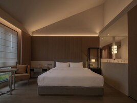 Quarto moderno com cama grande, mesas de cabeceira, uma cadeira e um espelho.