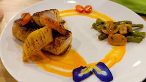 Prato com carne grelhada, legumes e um molho decorativo.