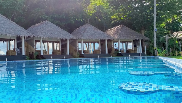 Uma piscina com água azul cristalina, rodeada por estruturas com telhados de palha.