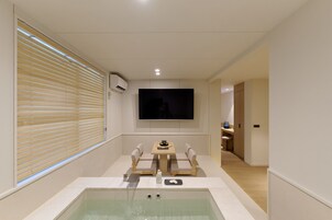 Um banheiro moderno com banheira, uma TV na parede e um espaço de estar com mesa e cadeiras.