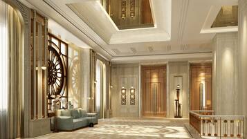Um hall espaçoso com um lustre imponente, um relógio de parede grande e uma escadaria moderna.